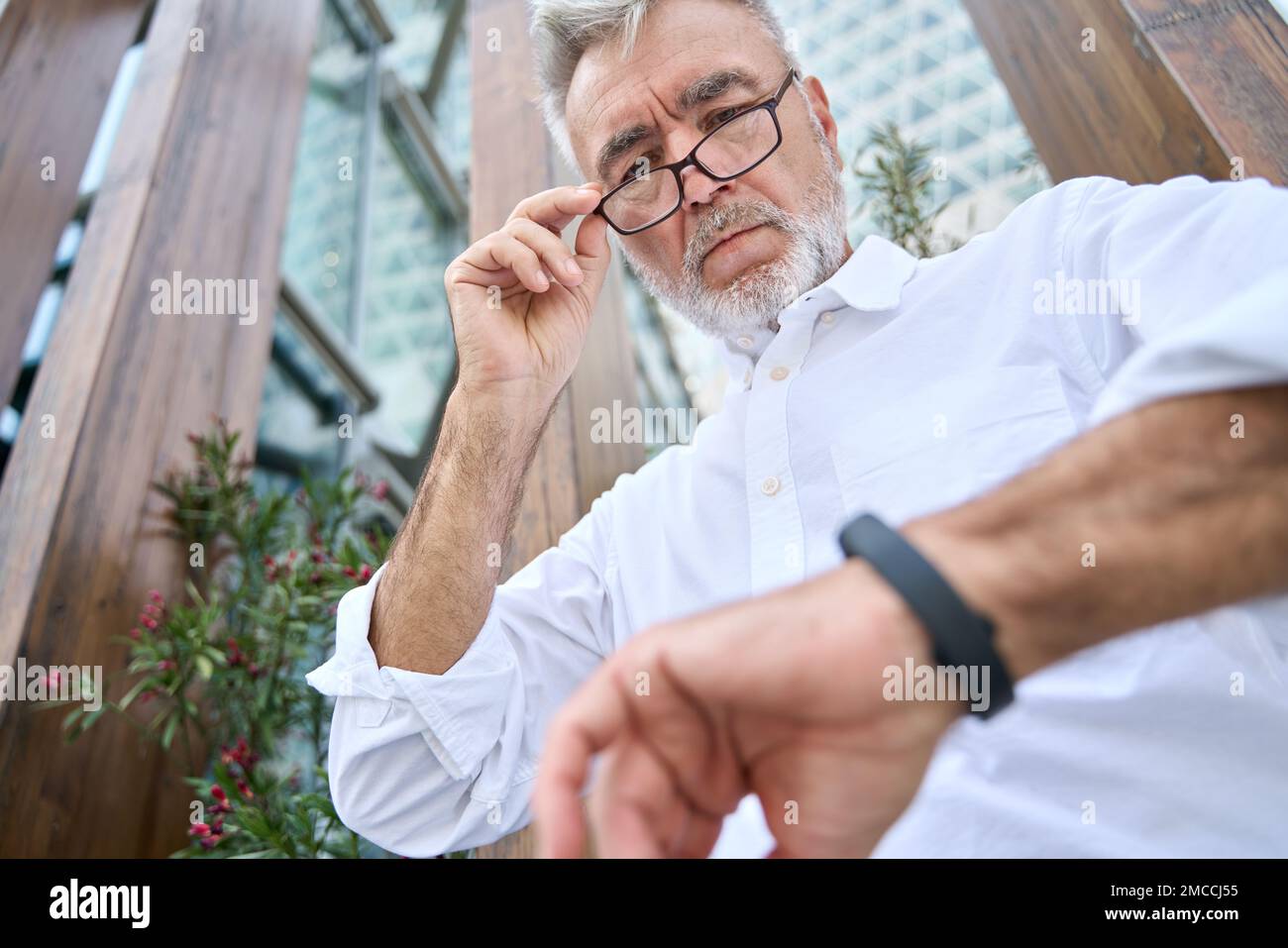 Busy older senior business man looking at wristwatch standing outdoors ...