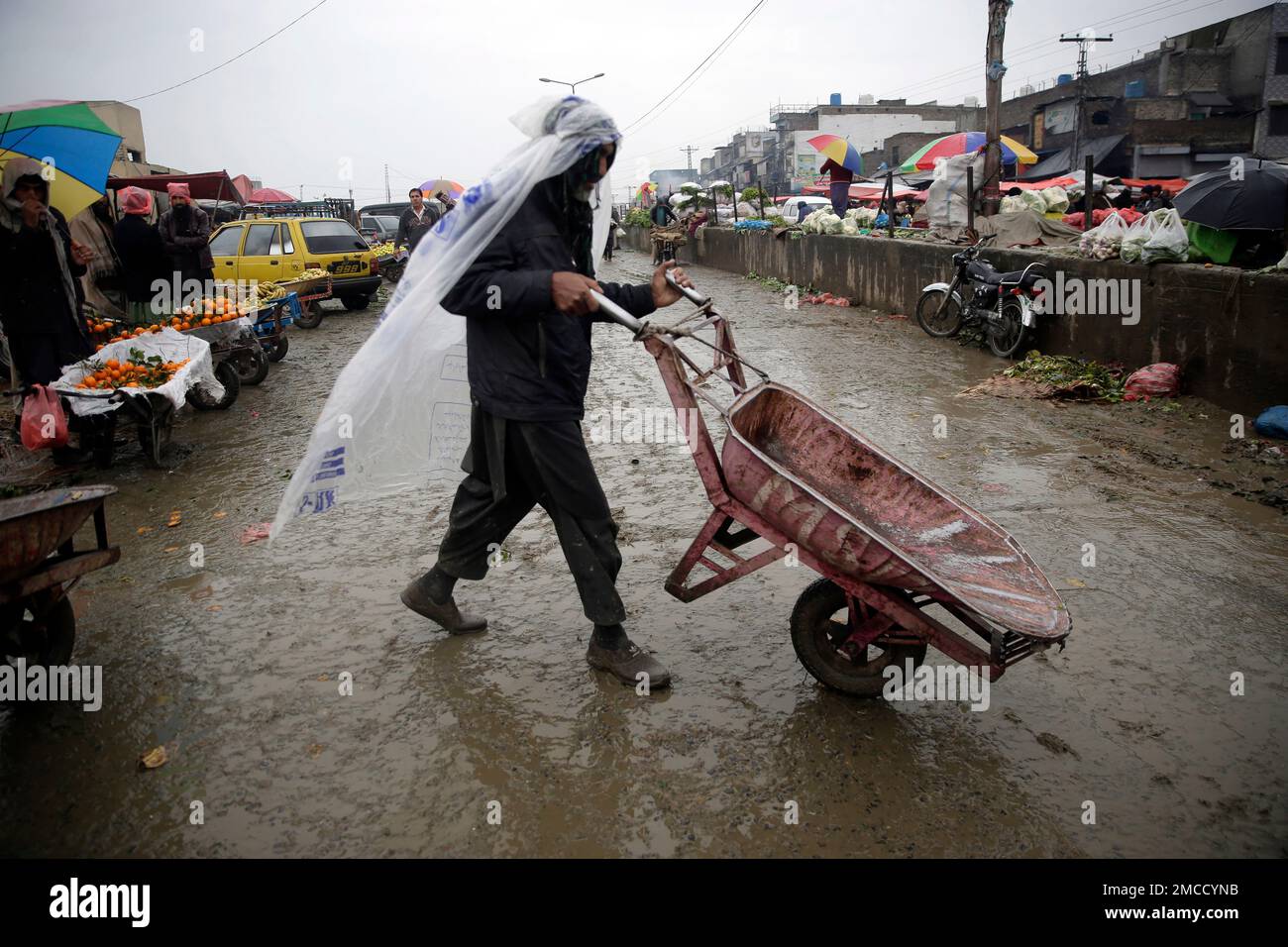 A man covers himself with a plastic sheet to protect from the rain at a ...