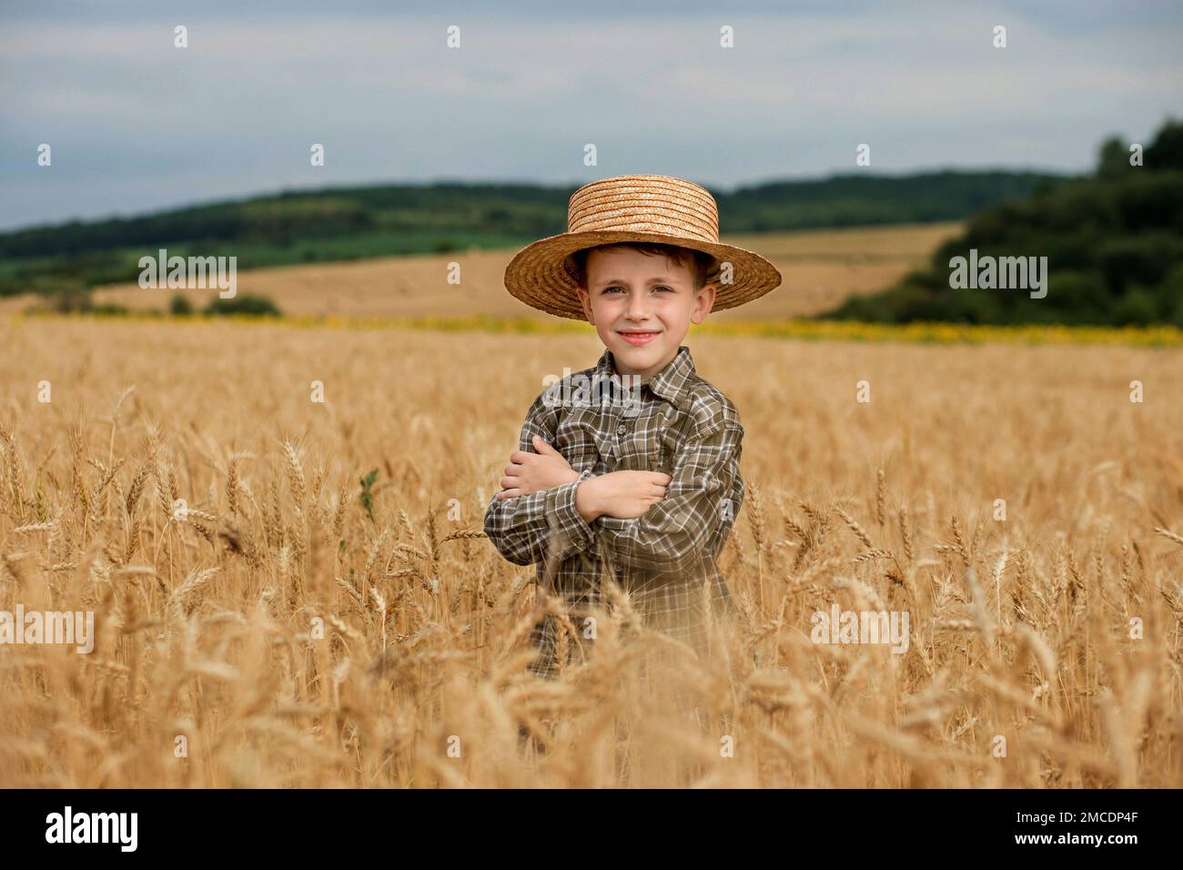 A smiling little farmer boy in a plaid shirt and straw hat poses for a ...