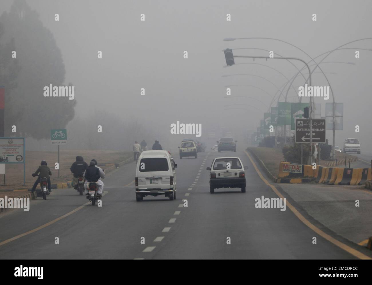 Vehicles and motorcyclists drive on a road in a heavy fog in Islamabad ...