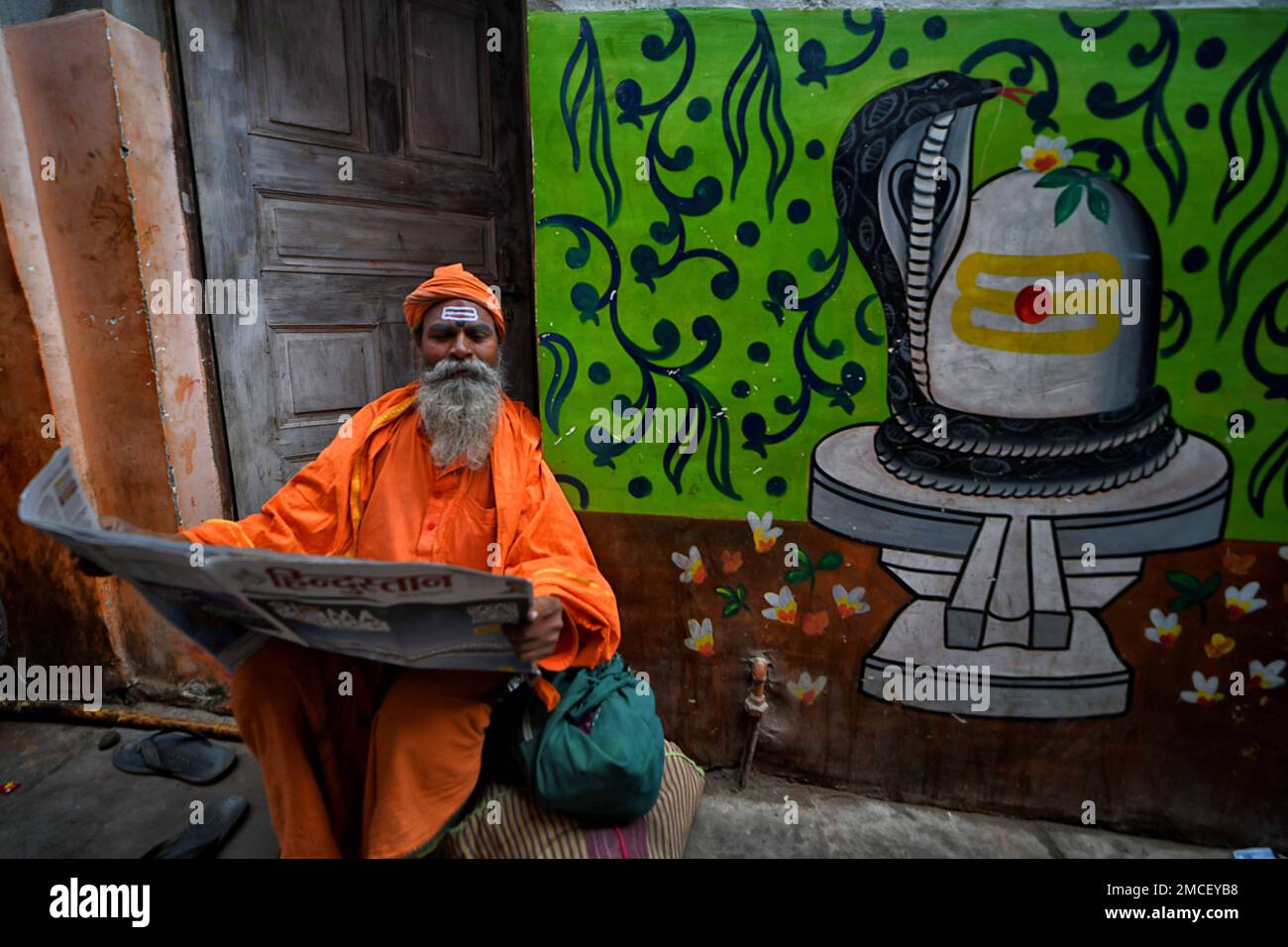 A Hindu priest seen reading newspapers besides a colorful graffiti wall ...