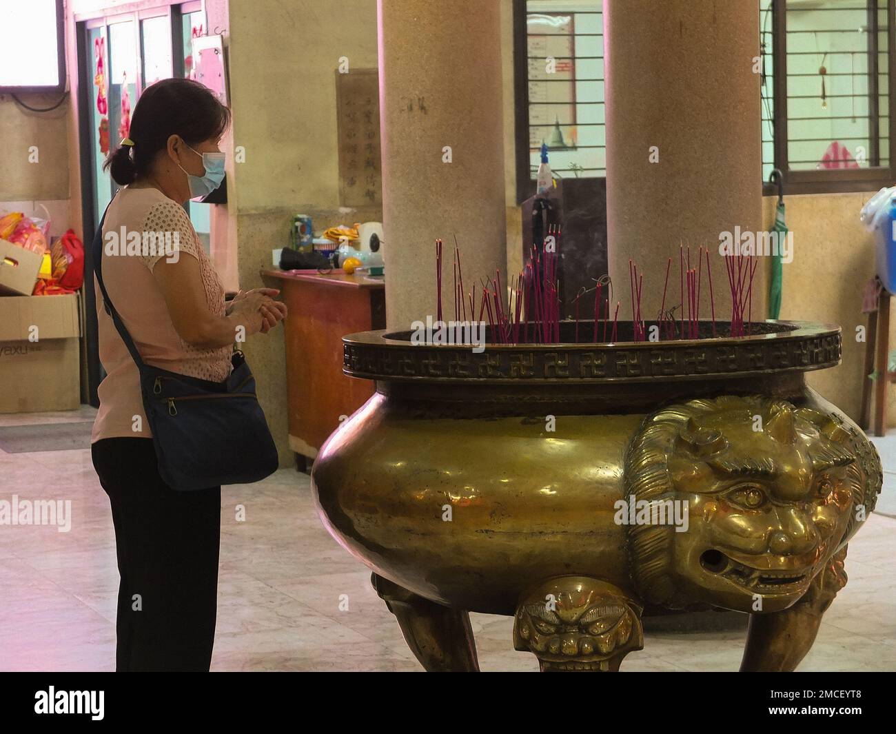 A Chinese woman lights an incense in a large ceremonial temple urn ...