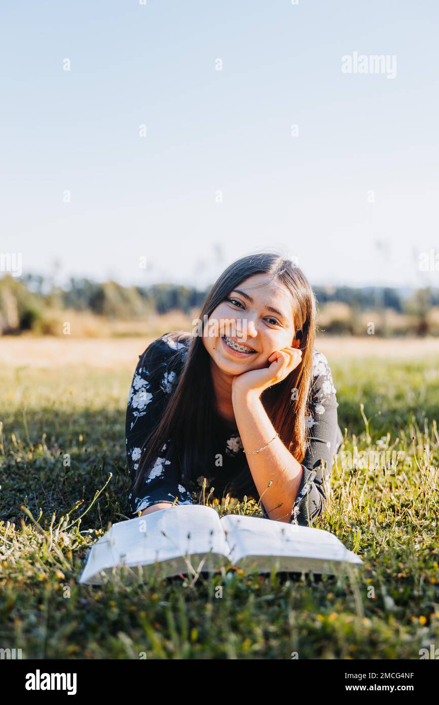 Smiling christian girl lying on the grass reading her bible, in the ...