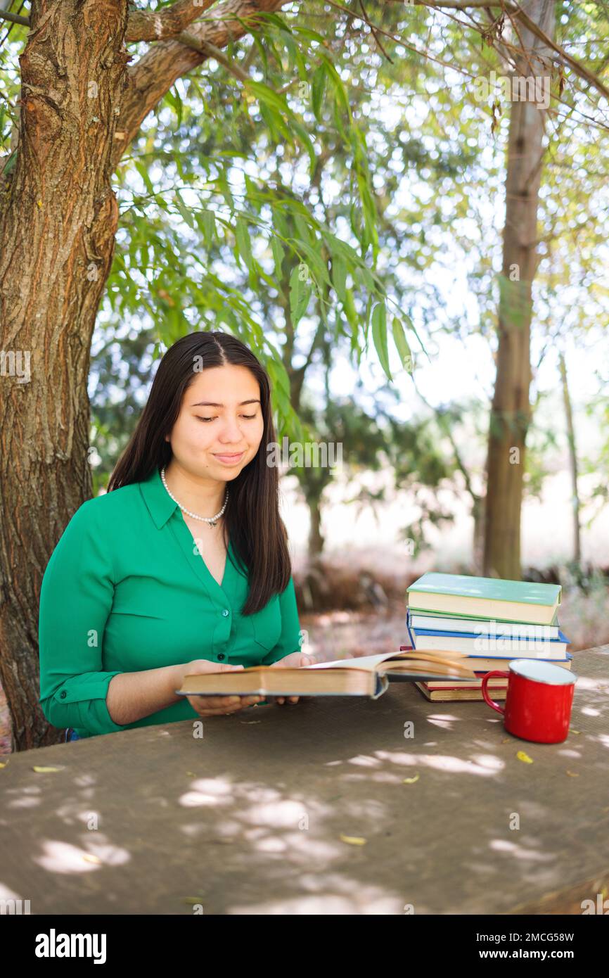 Cute young woman reading books in the field under a willow tree, with a ...