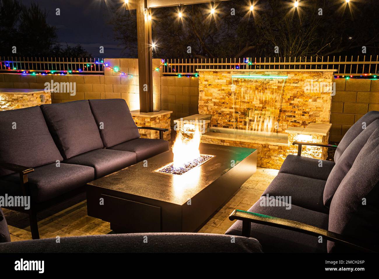 A resort style backyard at night with a waterfall, pergola, and a ...