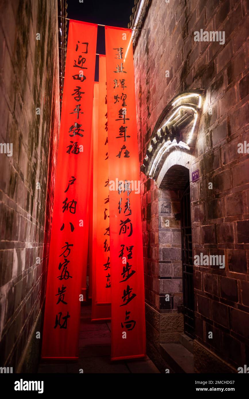 Red banners with Chinese script hanging in a narrow street at night ...