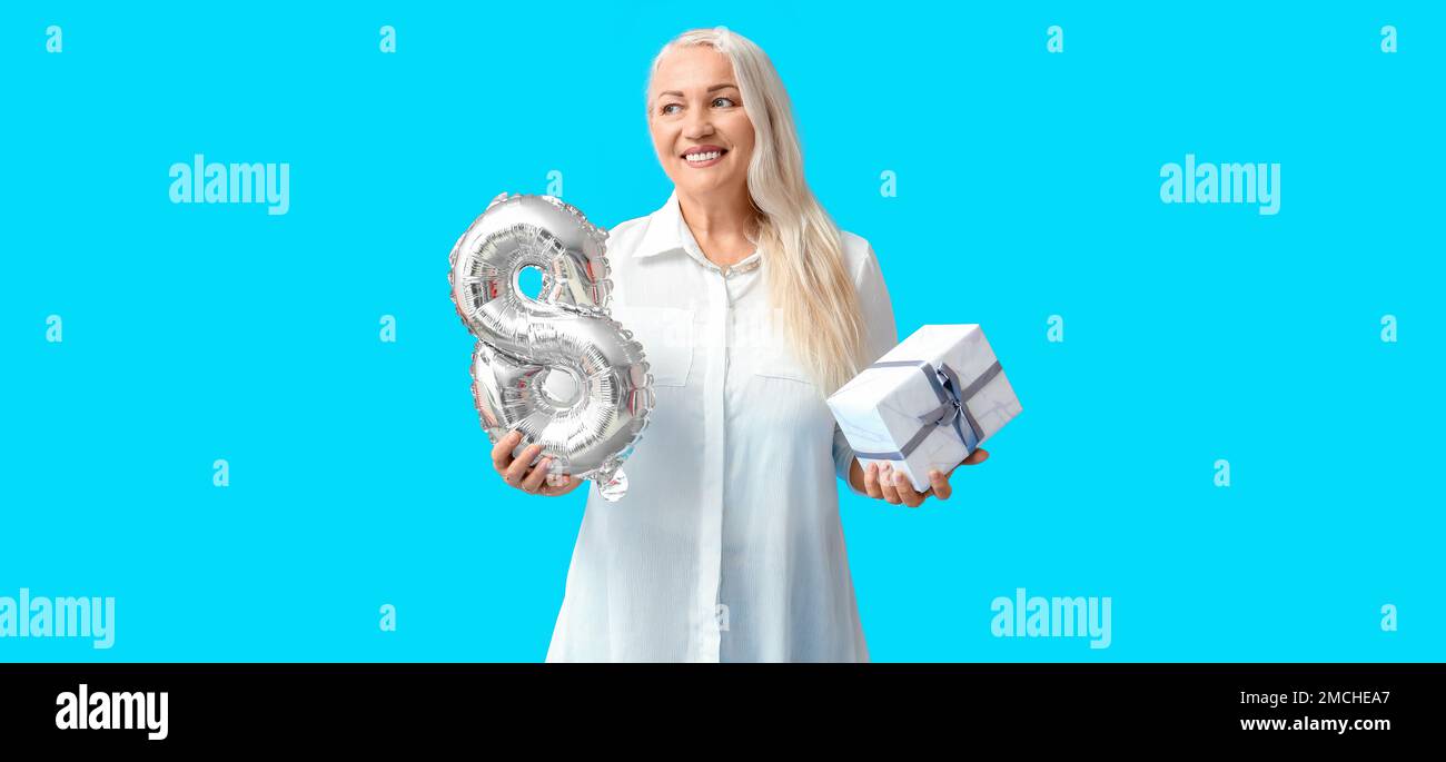 Smiling mature woman holding balloon and gift box on light blue ...