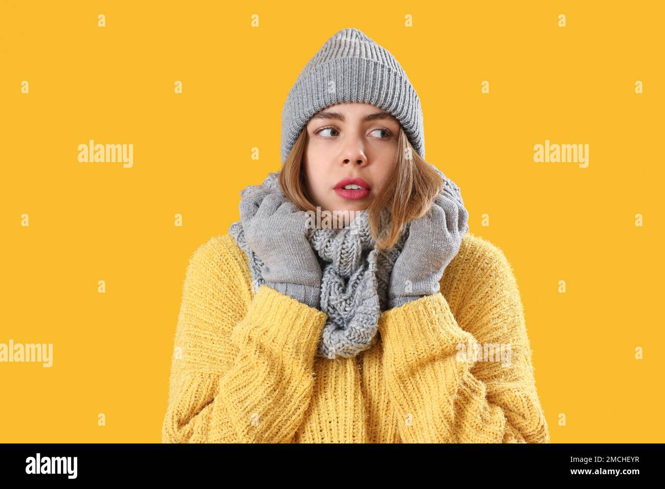 Frozen young woman in winter clothes on yellow background Stock Photo ...