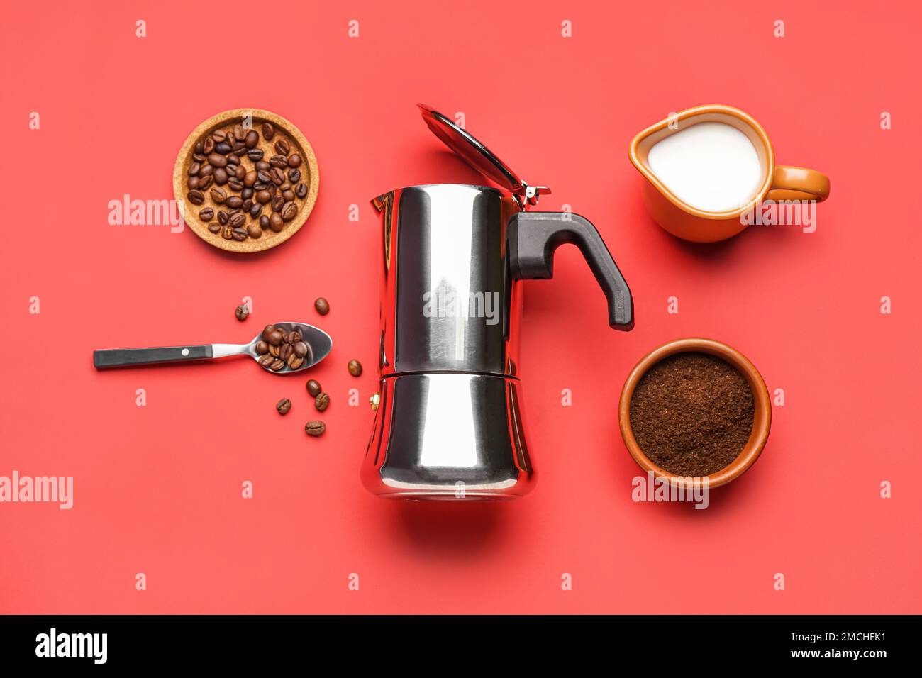 Geyser coffee maker, jug of milk, spoon, beans and melted coffee on red ...