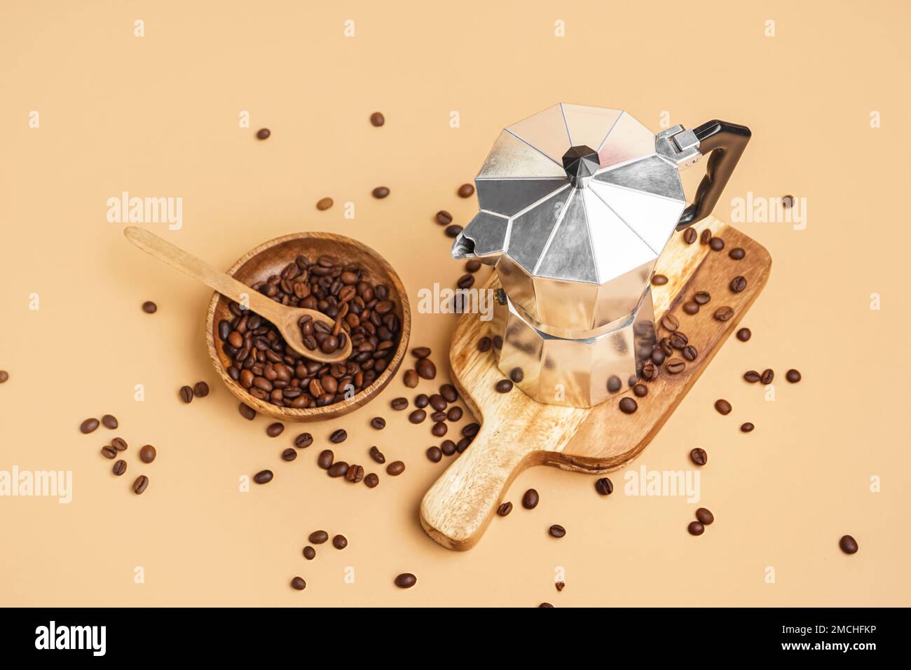 Cutting board with geyser coffee maker, beans and spoon on beige ...
