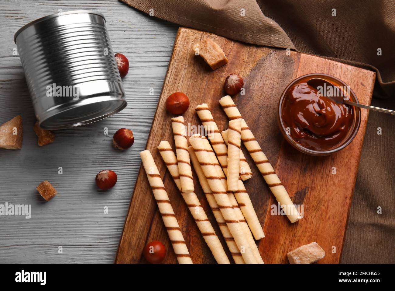 Wooden board with tasty wafer rolls, nuts, tin can and bowl of boiled ...