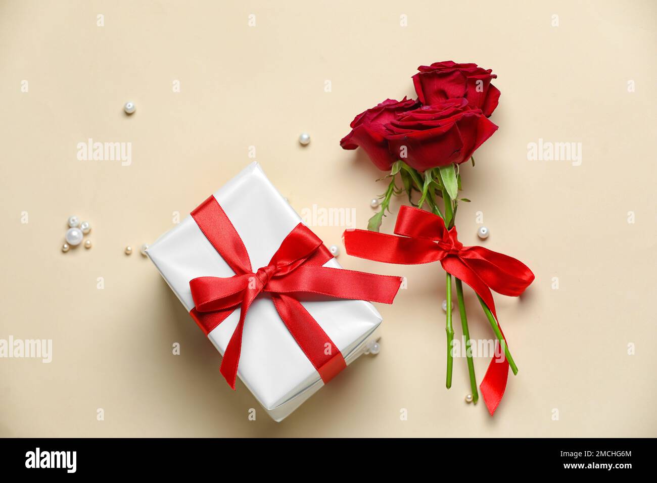 Gift box with beautiful bow, rose flower and beads on beige background ...