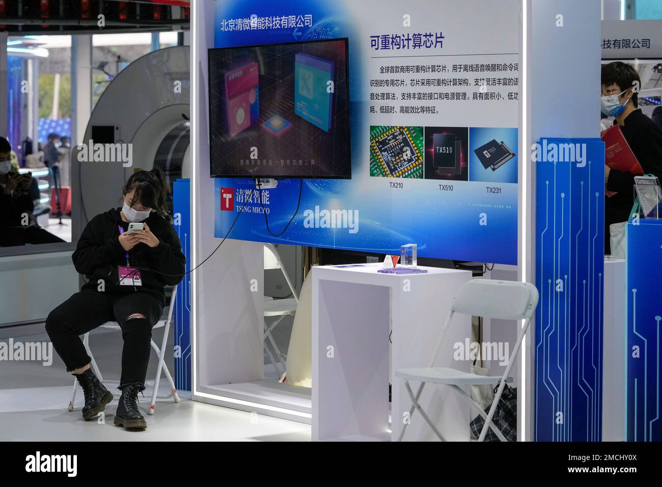 A woman wearing a face mask browses her smartphone at a booth ...