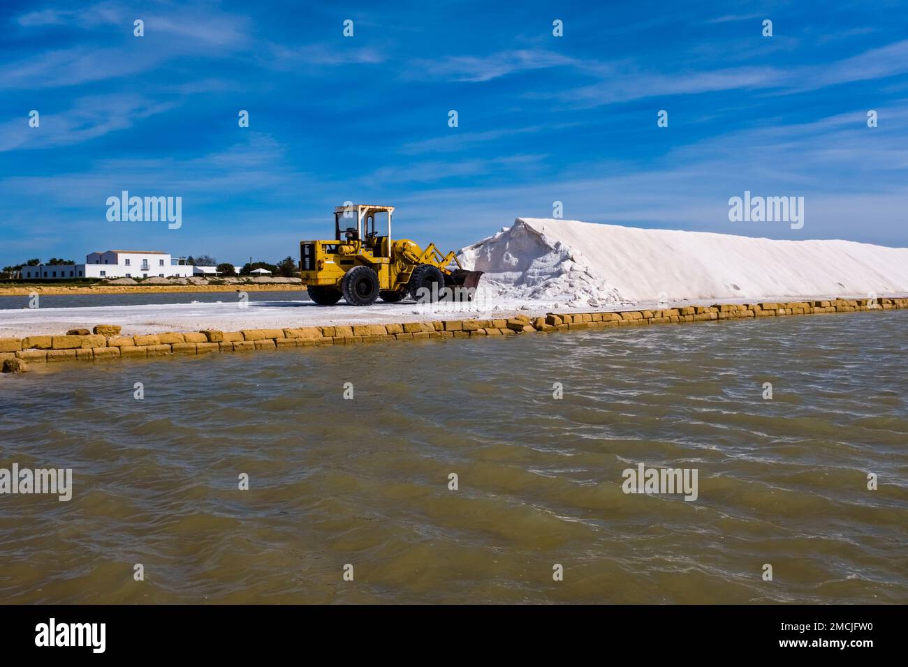 Piled salt, water basins and a yellow caterpillar in the Salina Culcasi ...