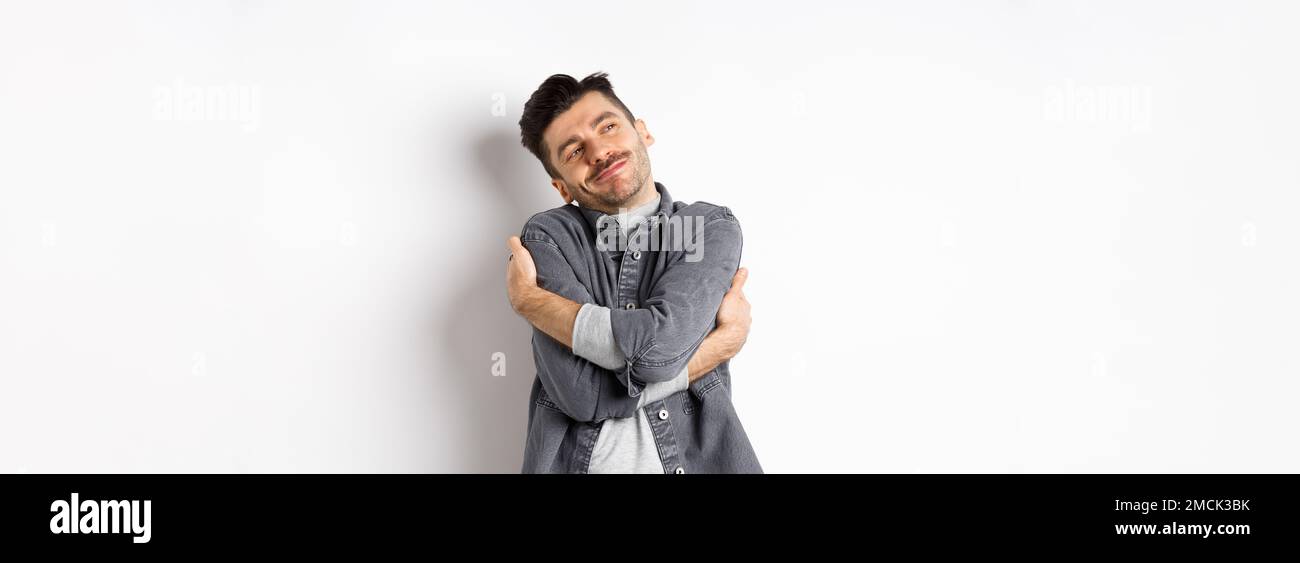 Happy romantic guy hugging himself with closed eyes and smile, loving ...