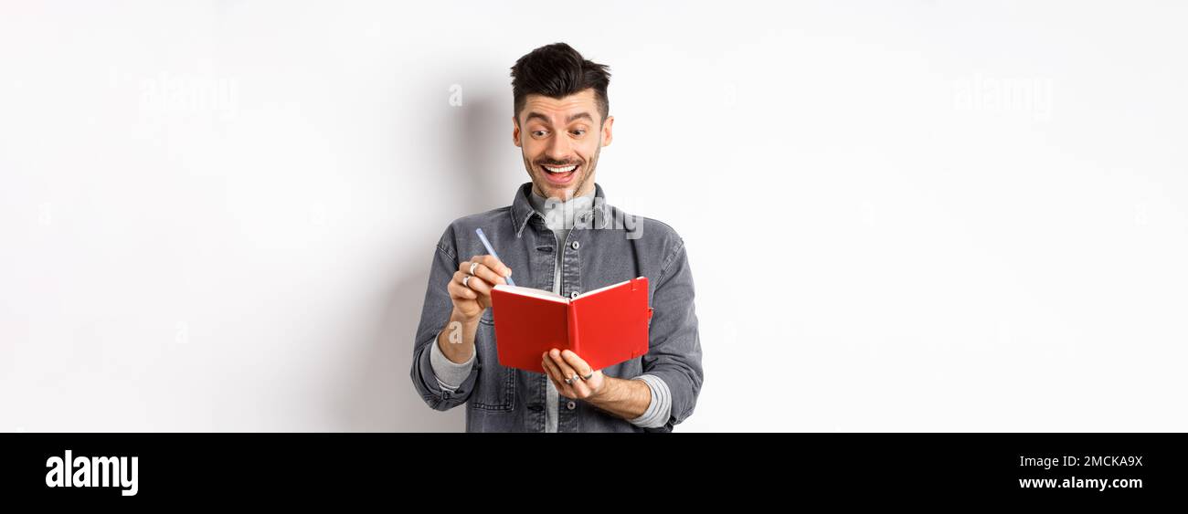 Excited guy writing in planner and smiling, writing down ideas in ...