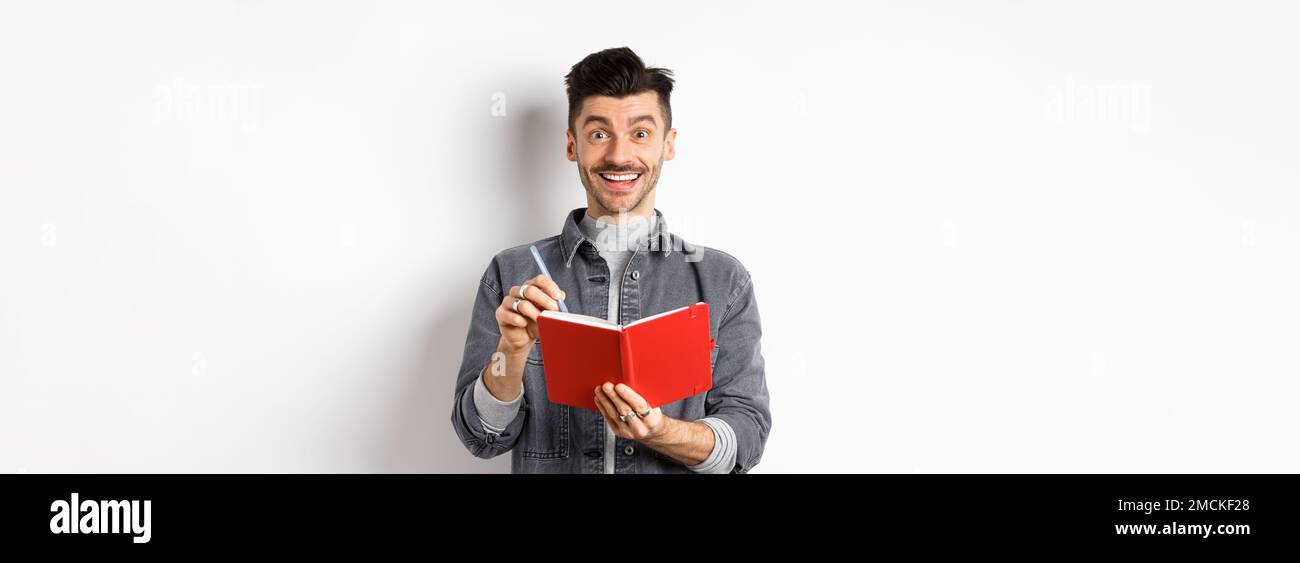 Creative young man smiling excited while taking notes, writing down ...