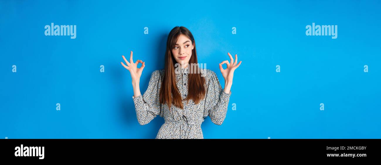Not bad. Pleased smiling woman with long hair, wearing dress, showing ...