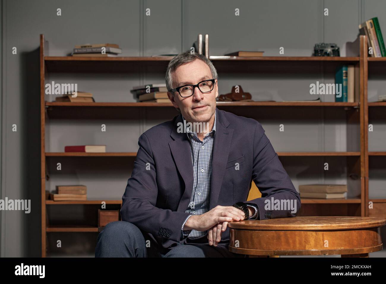 Happy grey haired man in blue suit and glasses is sitting in livingroom ...