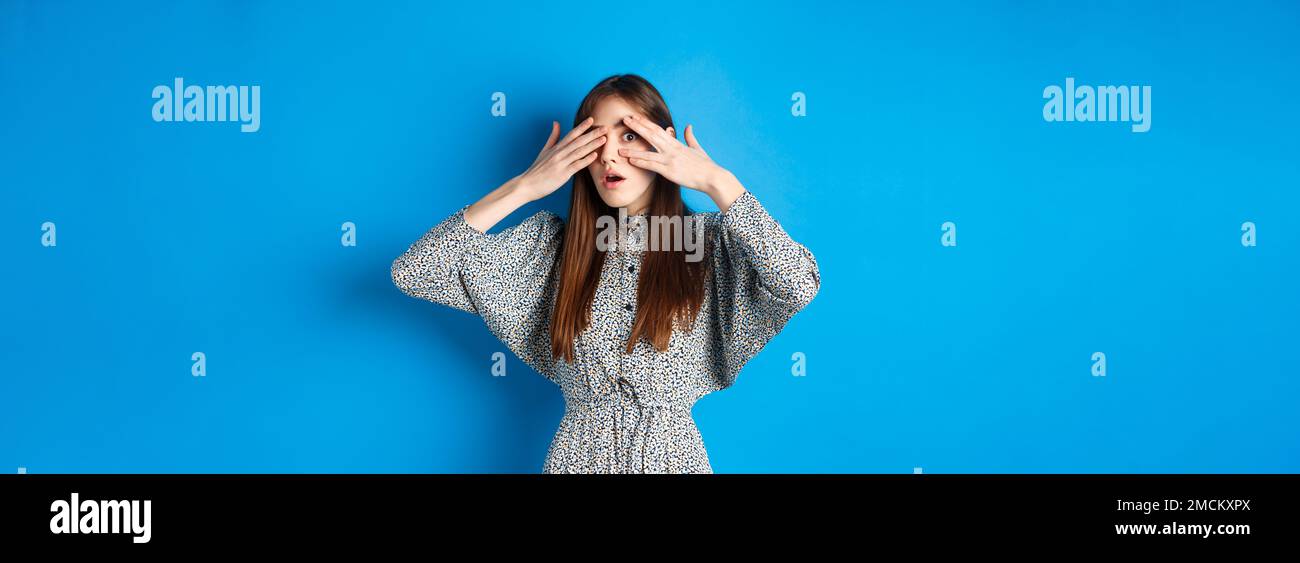 Intrigued young girl peeking through fingers with excitement, seeing ...