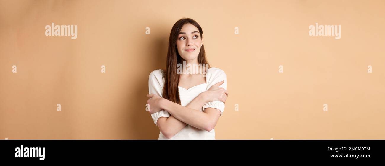 Romantic young girl dreaming, hugging herself and smiling at upper left ...