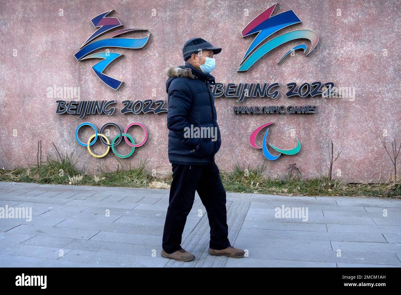 A man wearing a face mask walks past the logos for the Beijing 2022 ...