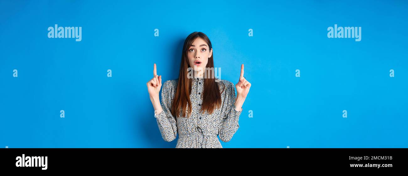 Surprised romantic girl in dress pointing, looking up with opened mouth ...