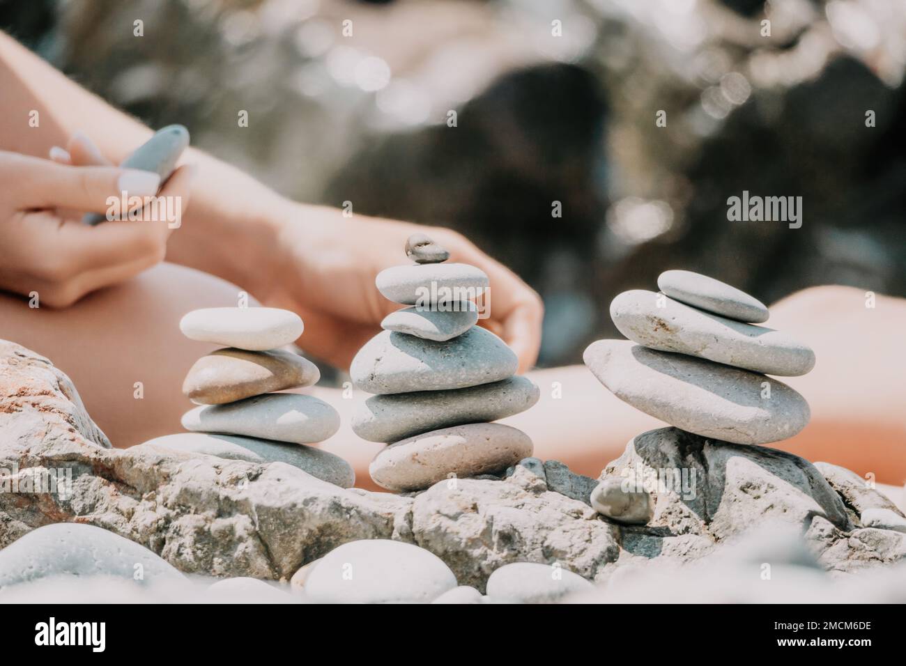 Woman with daughter bilds stones pyramid on seashore on a sunny day on ...