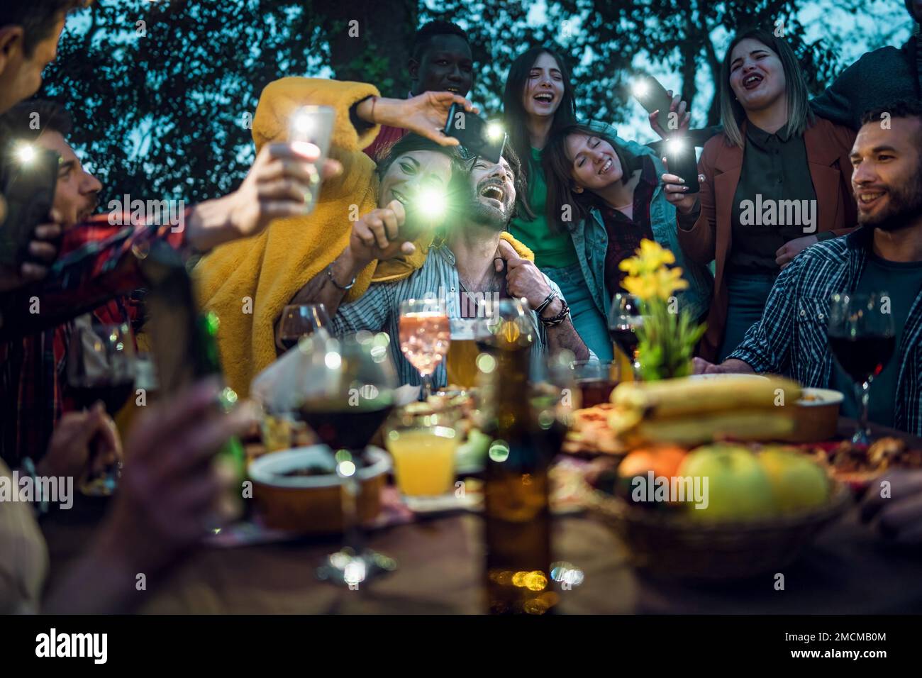 Diverse friends bonding over food, drinks, and song at sunset ...