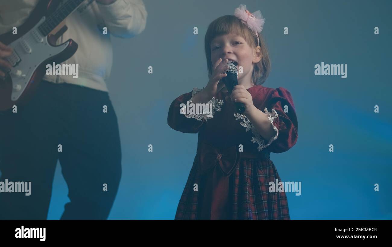 Little girl in vintage dress sings on stage, her father plays an ...