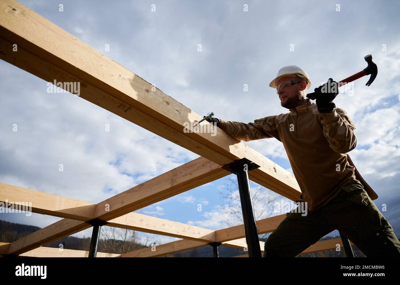 Man worker building wooden frame house on pile foundation. Carpenter ...