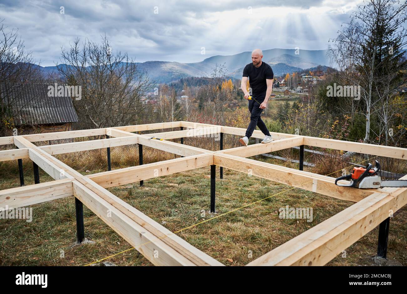 Man worker building wooden frame house on pile foundation in the ...