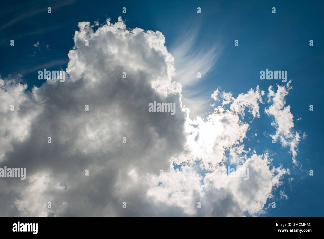 Blue skies and fluffy cloud hiding sun Stock Photo - Alamy