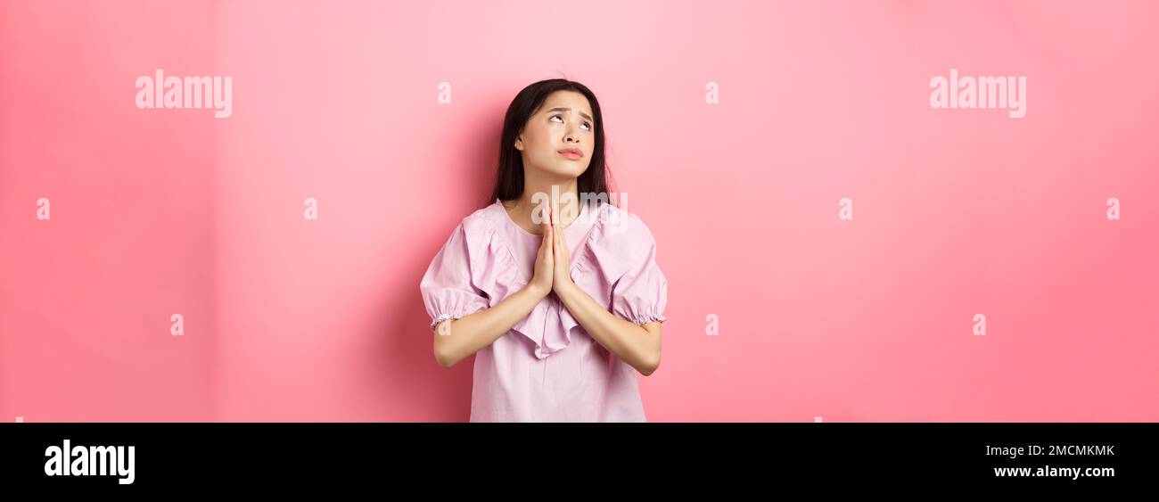 Hopeful asian girl praying god, looking up to plead or pray, making ...