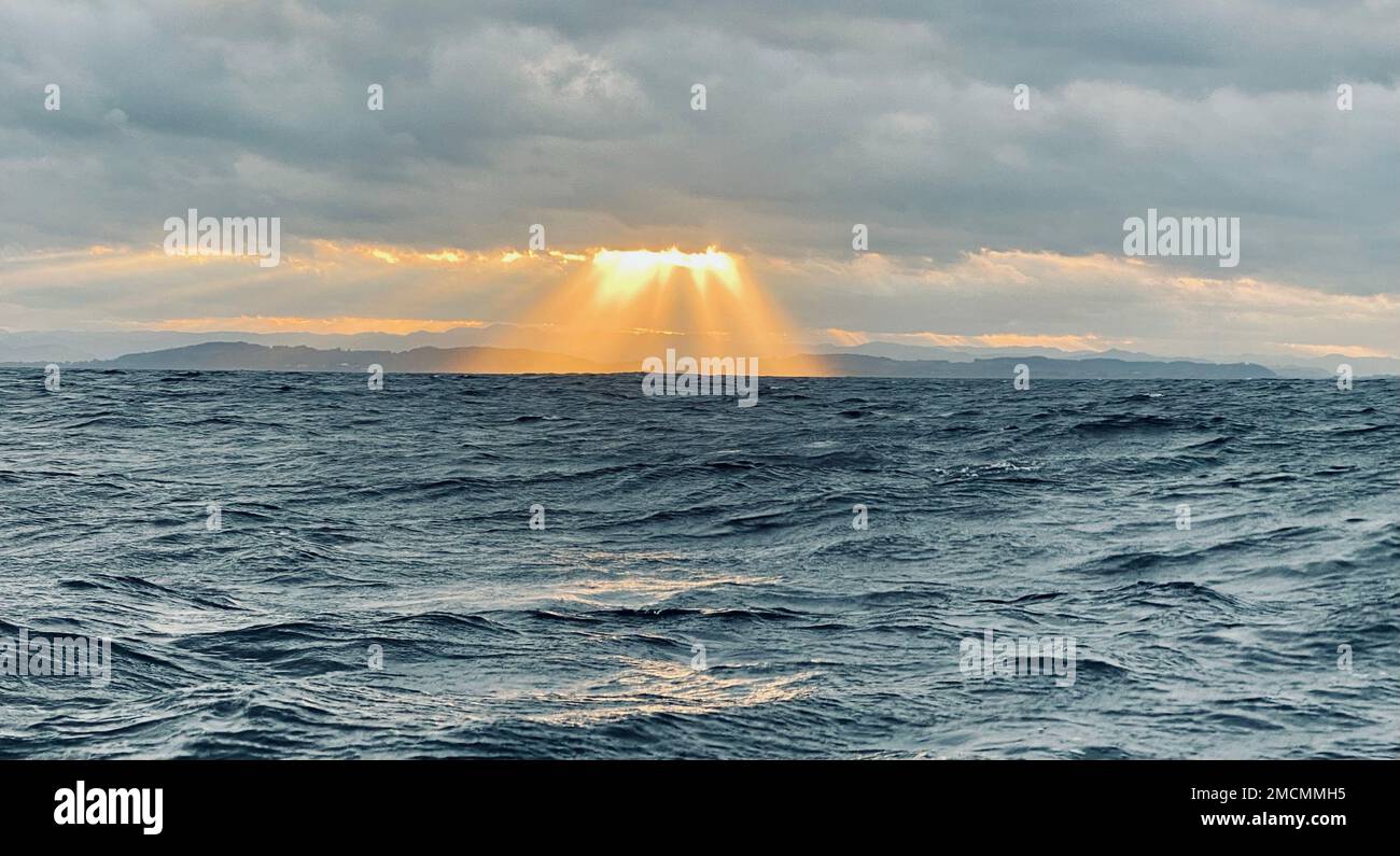 A scenic view of sunlight beaming through clouds above sea waves Stock ...