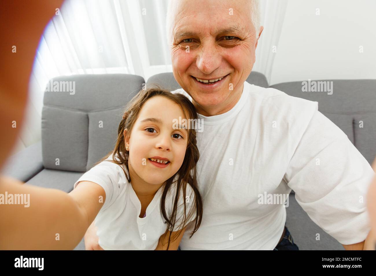 Cute little girl spending time with positive active grandpa in living ...