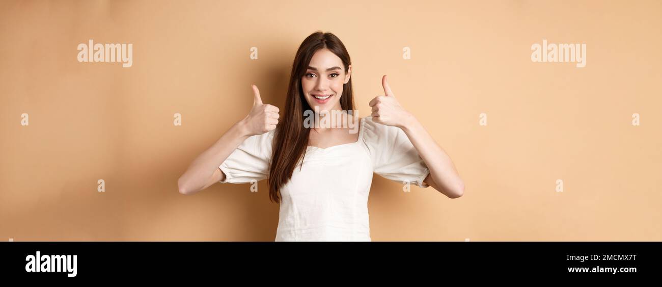 Very good. Happy and satisfied young woman showing thumbs-up, smiling ...