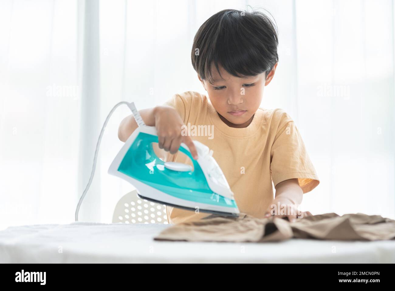 young happy boy iron his school uniform with iron on iron board at home ...
