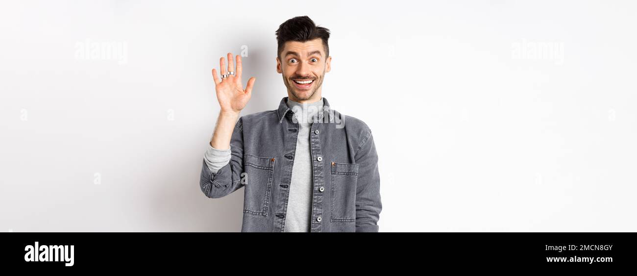 Friendly stylish man saying hello and waiving hand, smiling cheerful ...
