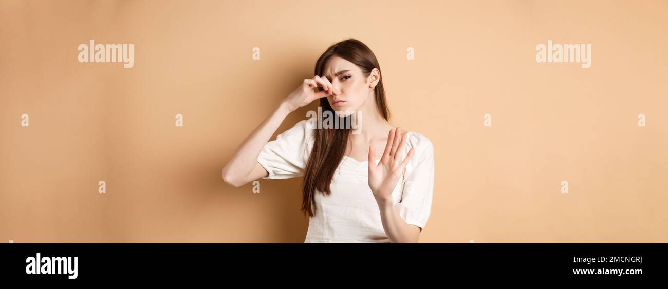 Displeased woman plug her nose from bad smell, showing stop gesture and ...