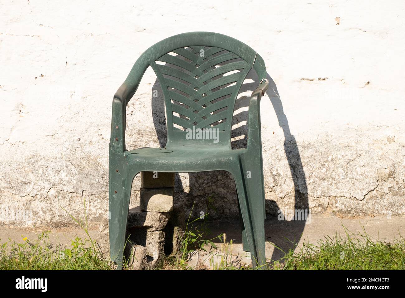 a plastic old broken chair stands on the background of a white wall of ...