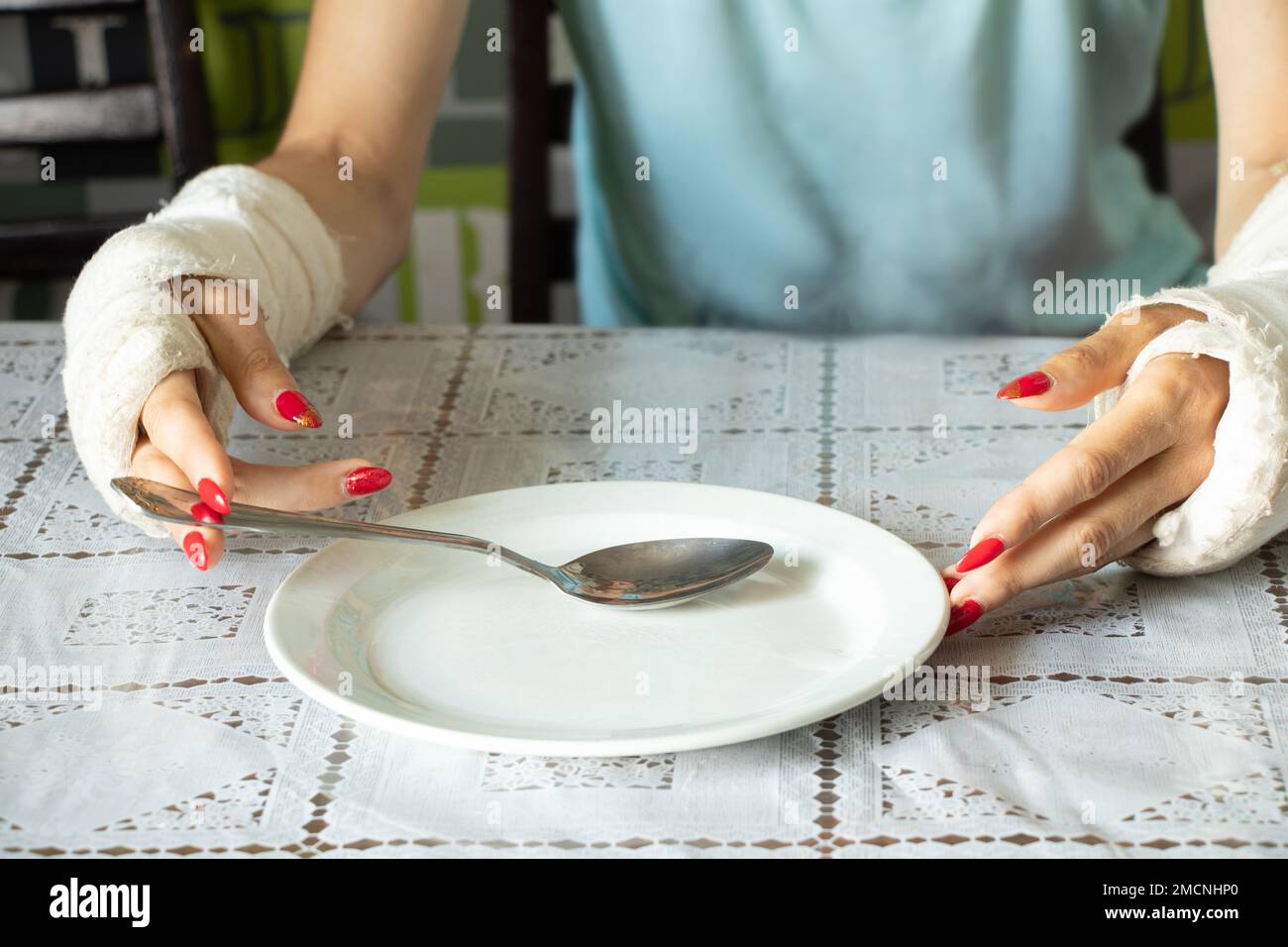 a girl with two broken arms in a cast holds a spoon to a plate at the ...