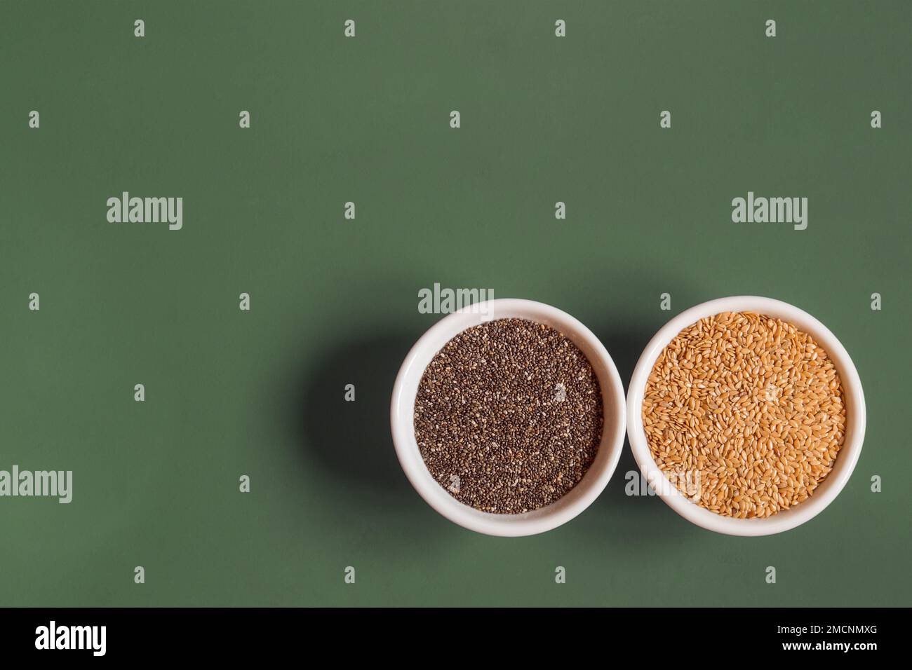 Top view of whole chia and flax seeds in small round white ceramic bowls, side by side, on a ...