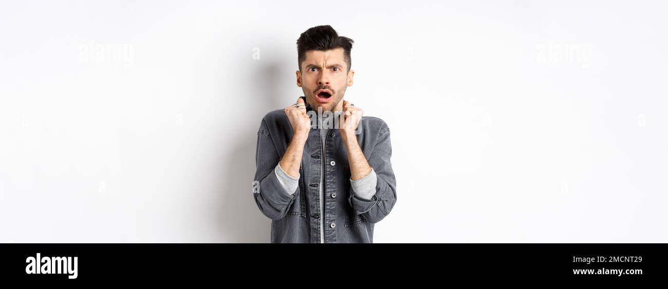 Shocked young man look confused and offended, gasping and frowning at ...