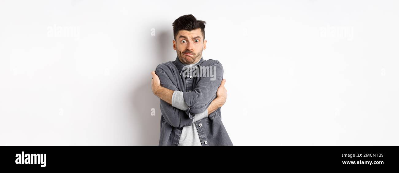 Funny young man hugging himself and grimacing, feeling embarrassed and ...