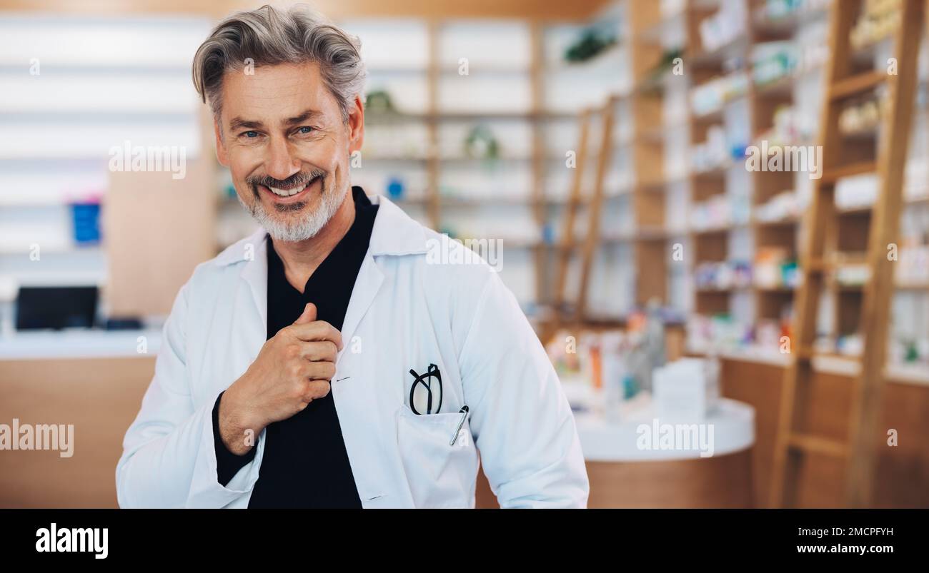 Doctor standing in a pharmacy in a lab coat. Mature healthcare worker ...