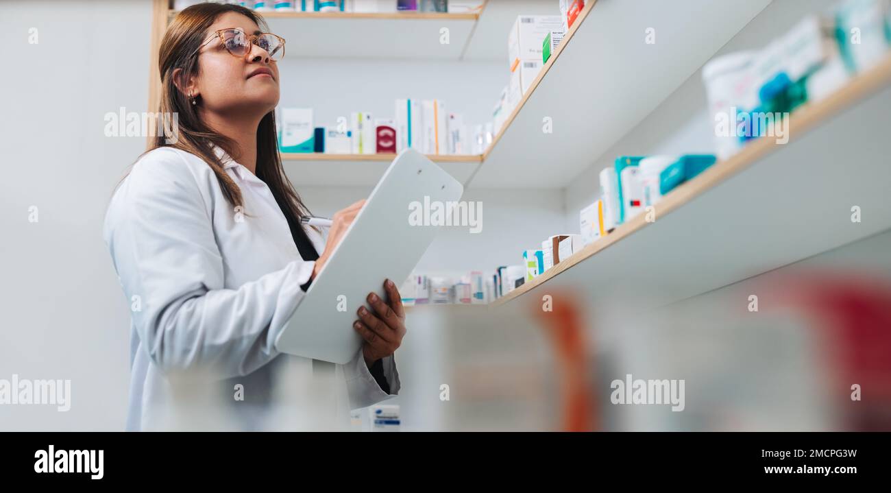 Female pharmacist writing on a clipboard while doing a stock take in a ...