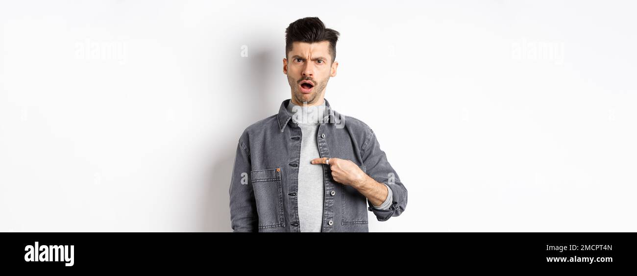 Offended young man being accused, frowning and pointing at himself ...