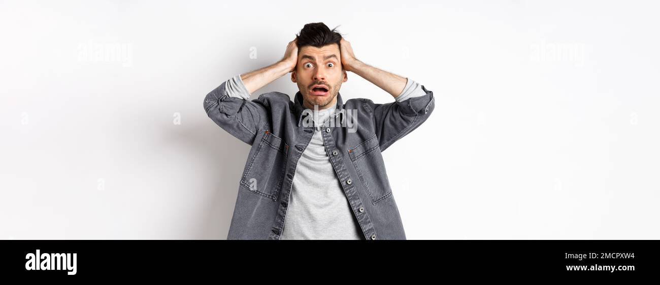 Alarmed young man grab head and pop eyes at camera, looking worried and ...