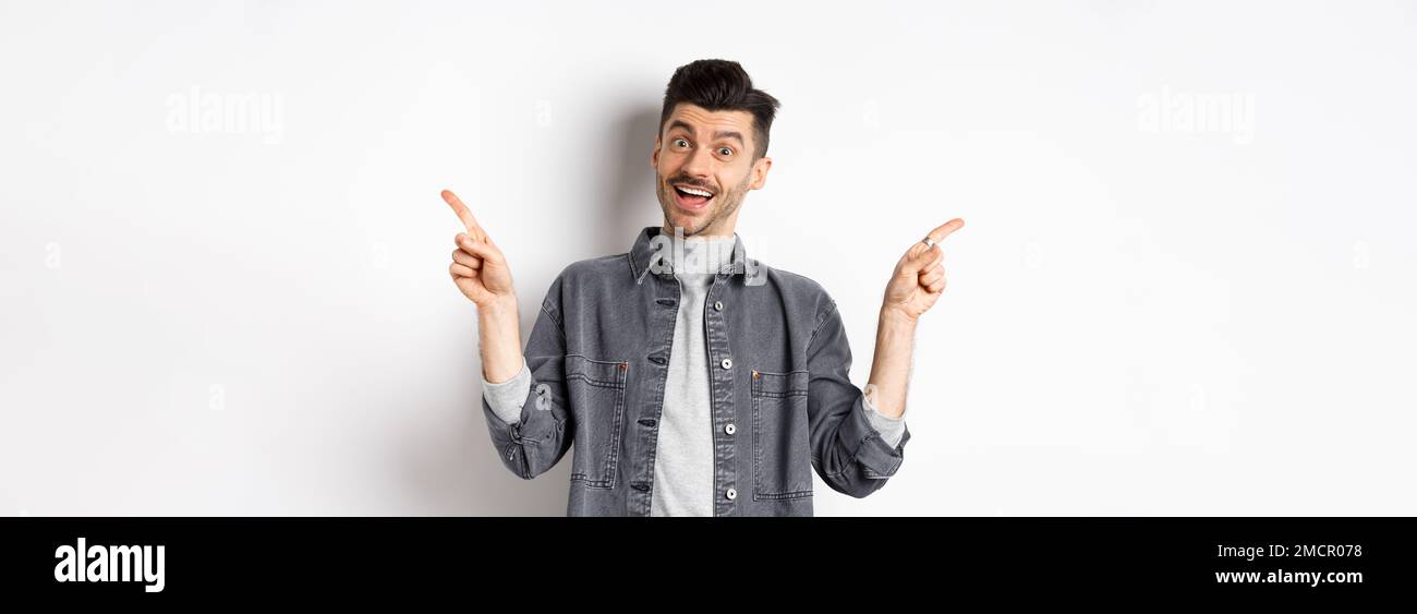 Cheerful smiling man pointing fingers sideways, showing left and right ...